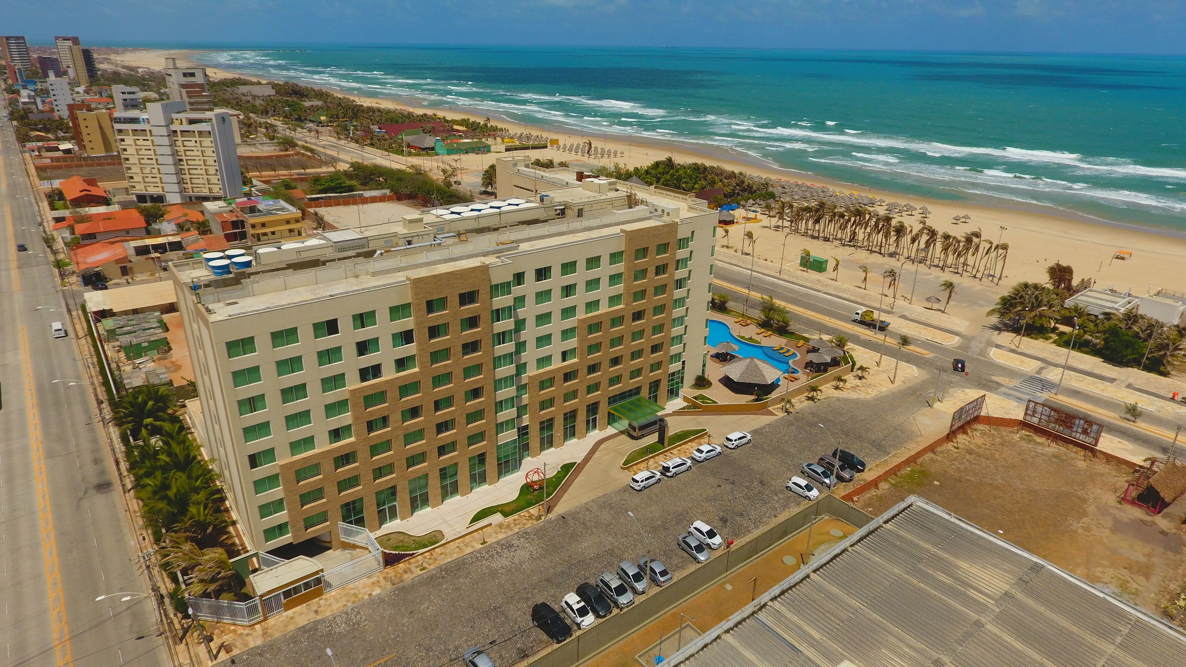 Um hotel com piscina, vários estacionamentos e vista para a praia e oceano.