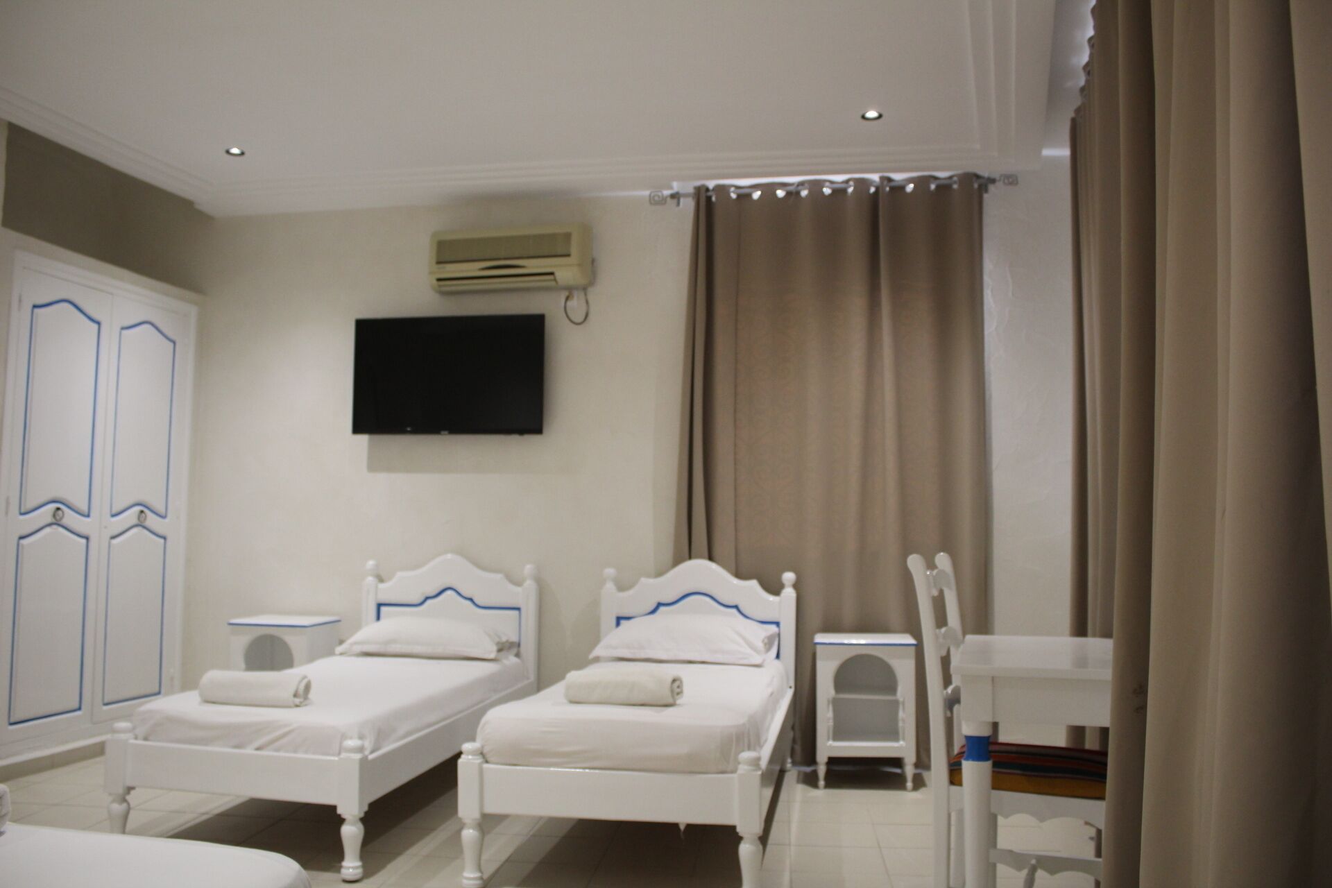 Quarto de hotel com duas camas de solteiro, televisão fixada na parede e janela com cortinas.