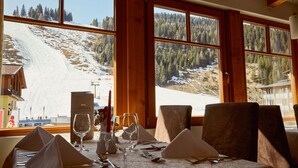 Uma sala de jantar com uma mesa posta para dois, grandes janelas com vista para uma montanha nevada e floresta.