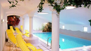 Piscina interior com espreguiçadeiras listradas de amarelo e chão de azulejos.
