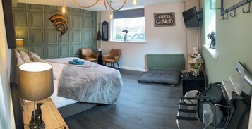 Quarto de hotel com cama, duas cadeiras, escrivaninha, bicicleta e janela com vista para a rua.