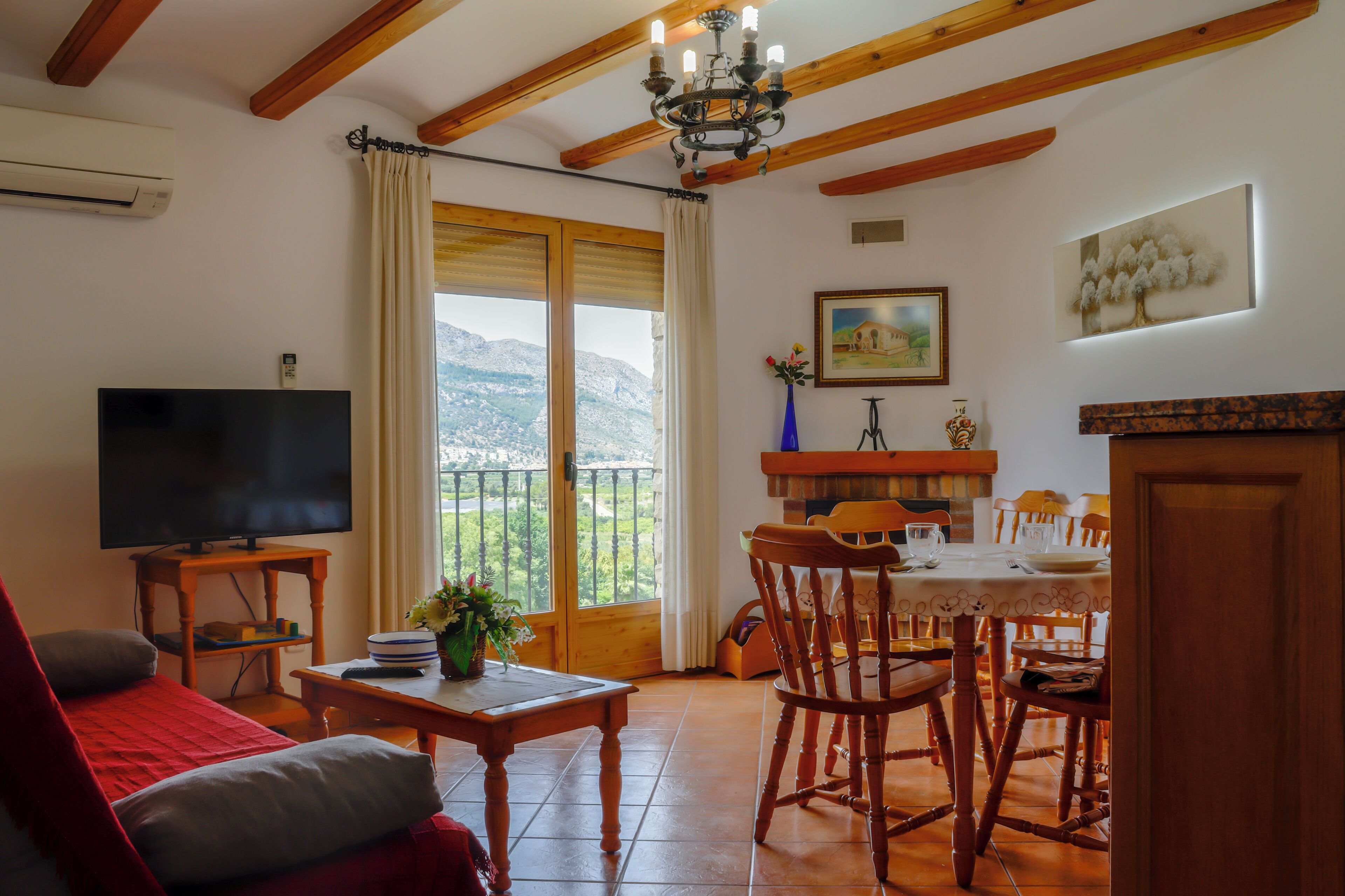 Uma sala de estar com televisão, uma mesa de jantar com cadeiras, um sofá e uma varanda com vista para as montanhas.