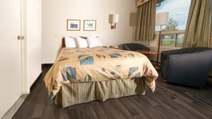 Quarto de hotel com uma cama grande, uma escrivaninha, uma cadeira e uma janela com cortinas.