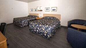 Quarto de hotel com duas camas, uma escrivaninha, uma cadeira e uma mesinha.