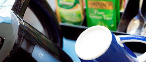Máquina de café com duas canecas azuis e um saquinho de chá verde.