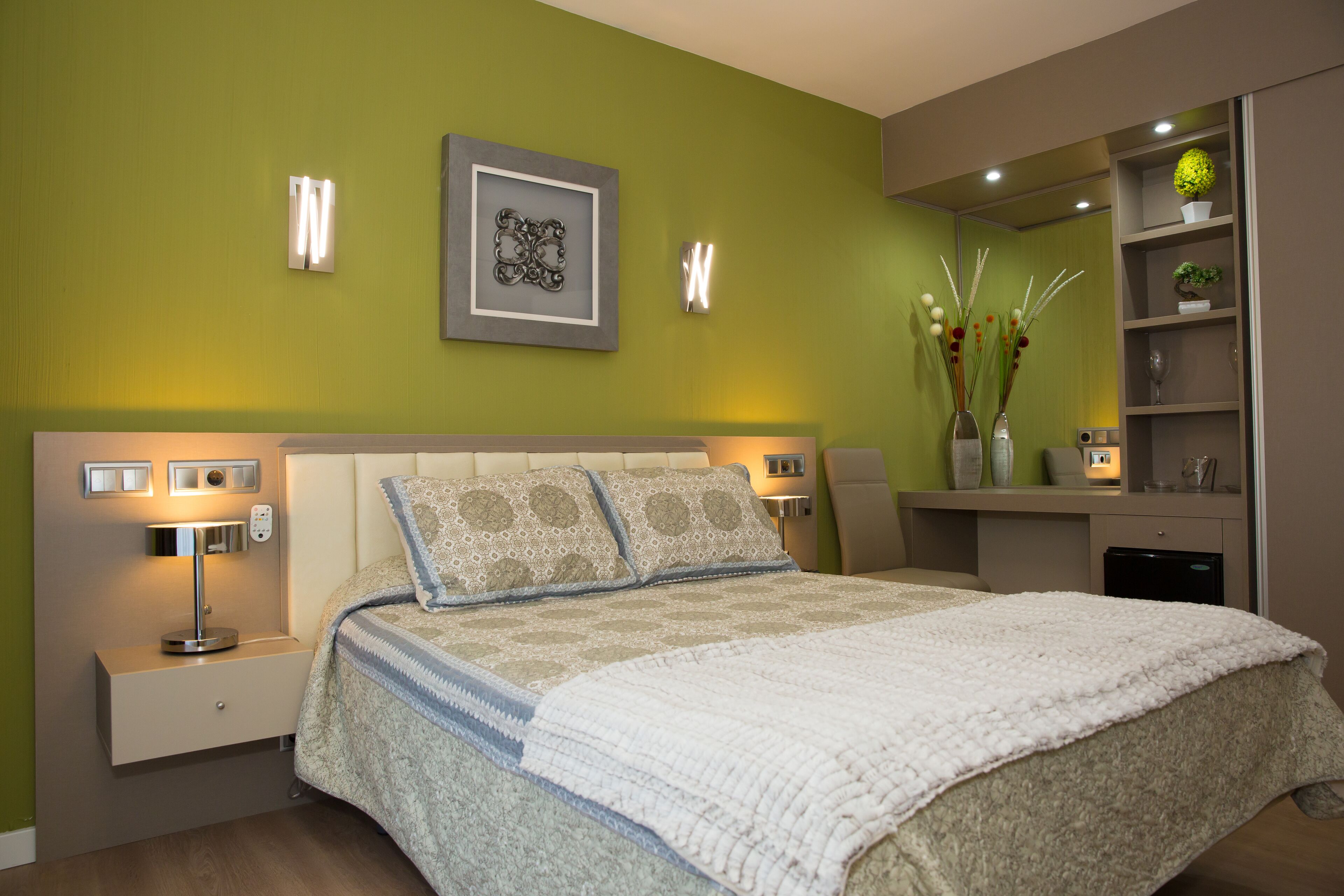 Um quarto moderno com cama, abajures, mesa de cabeceira, cômoda e espelho.