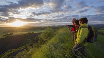 Um grupo de pessoas caminhando numa colina gramada, com um pôr do sol ao fundo.