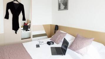 Quarto de hotel com cama, um laptop, fones de ouvido e um vestido preto pendurado na parede.