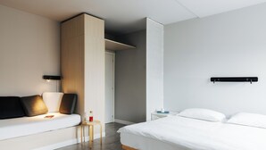 Quarto de hotel moderno com cama, sofá, pequena mesa e guarda-roupa.