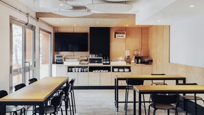 Um café moderno com uma longa mesa de madeira e cadeiras, uma máquina de café e um sinal indicando um aparelho de ar condicionado.