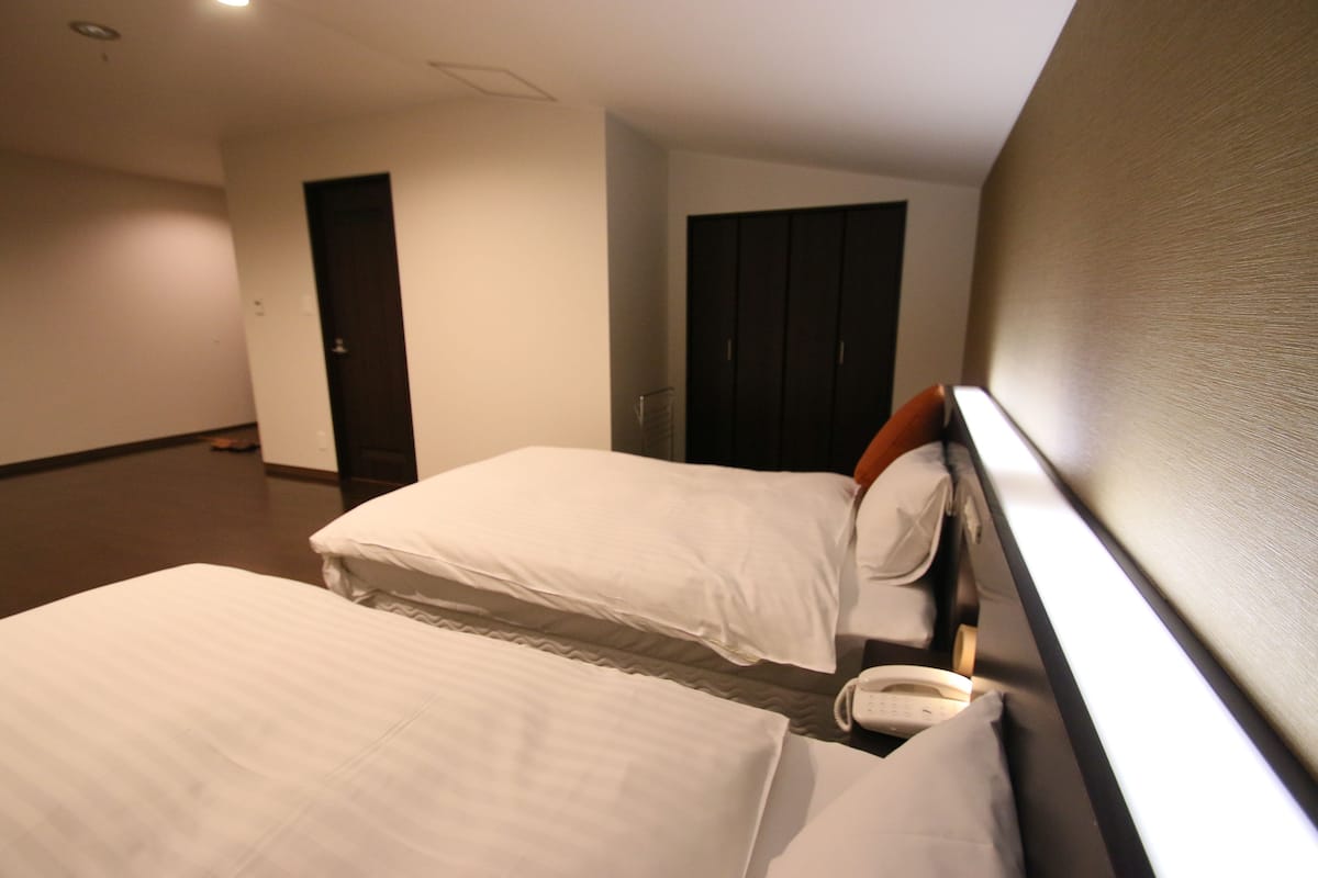 Quarto de hotel com duas camas, telefone ao lado da cama e um guarda-roupa.