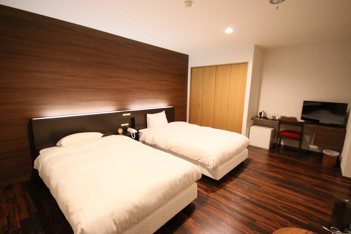 Quarto de hotel moderno com duas camas, uma secretária, uma televisão e um guarda-roupa.