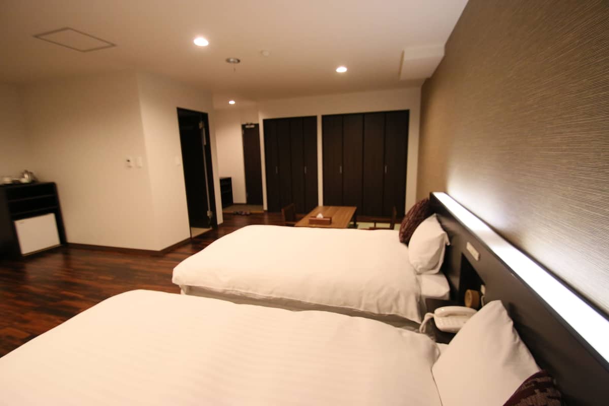 Quarto de hotel com duas camas, uma escrivaninha, uma cadeira, um guarda-roupa e uma mesinha.