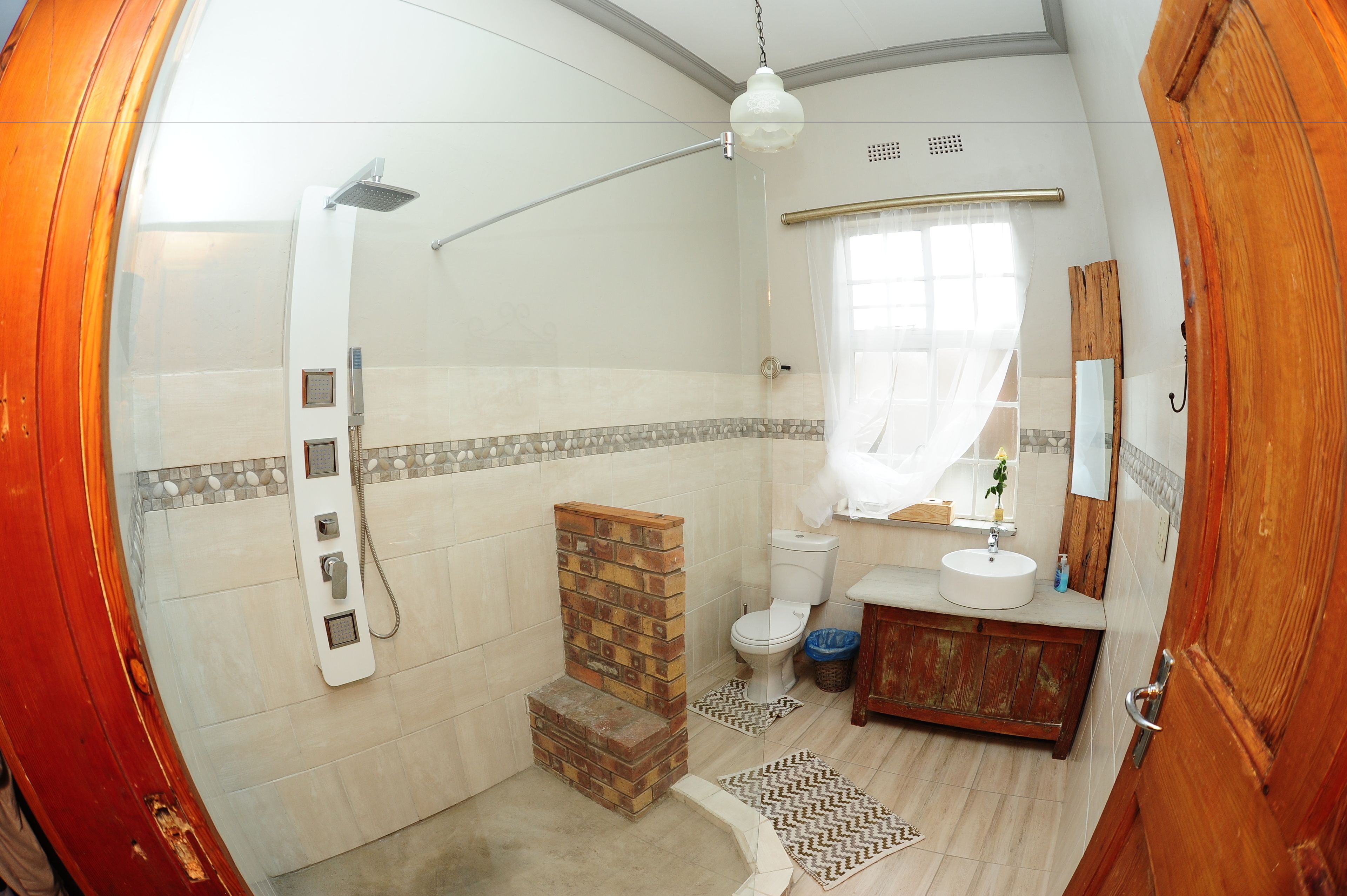 Casa de banho com chuveiro, sanita, lavatório e um banco de madeira.