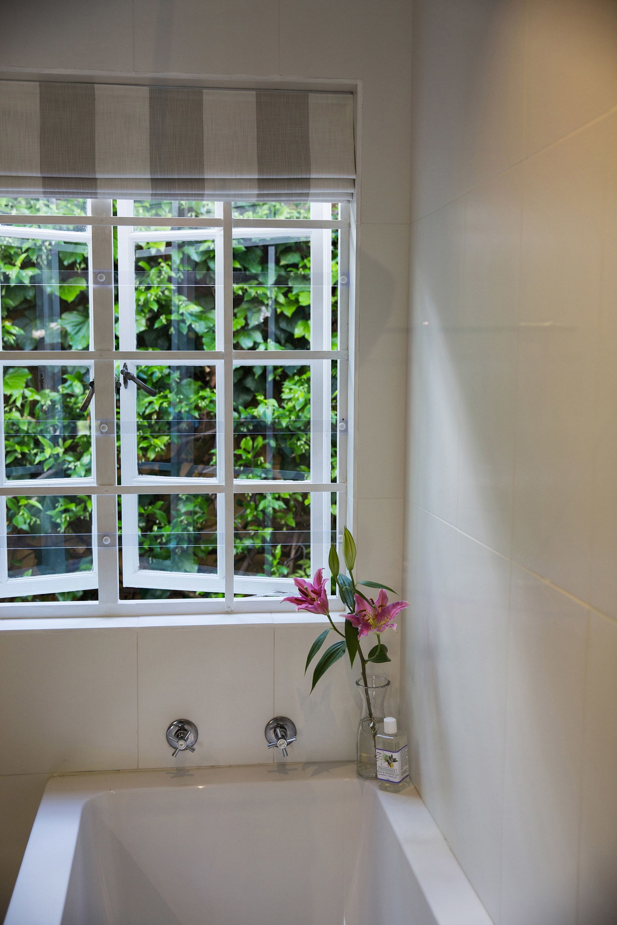 Um banheiro com banheira, uma janela com persianas e um vaso com flores.