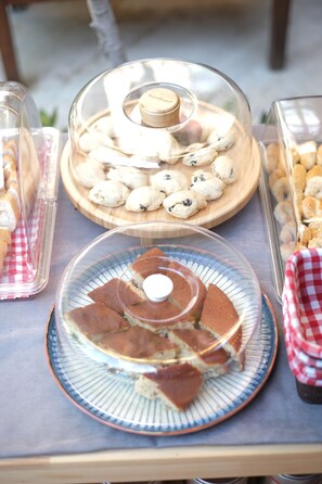 Uma mesa com diversos alimentos, incluindo um prato com biscoitos, um pão de forma e um recipiente com doces.