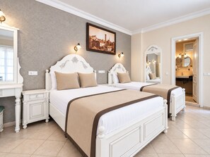 Quarto de hotel com duas camas, um espelho grande, uma pintura na parede e um banheiro visível através de uma porta aberta.