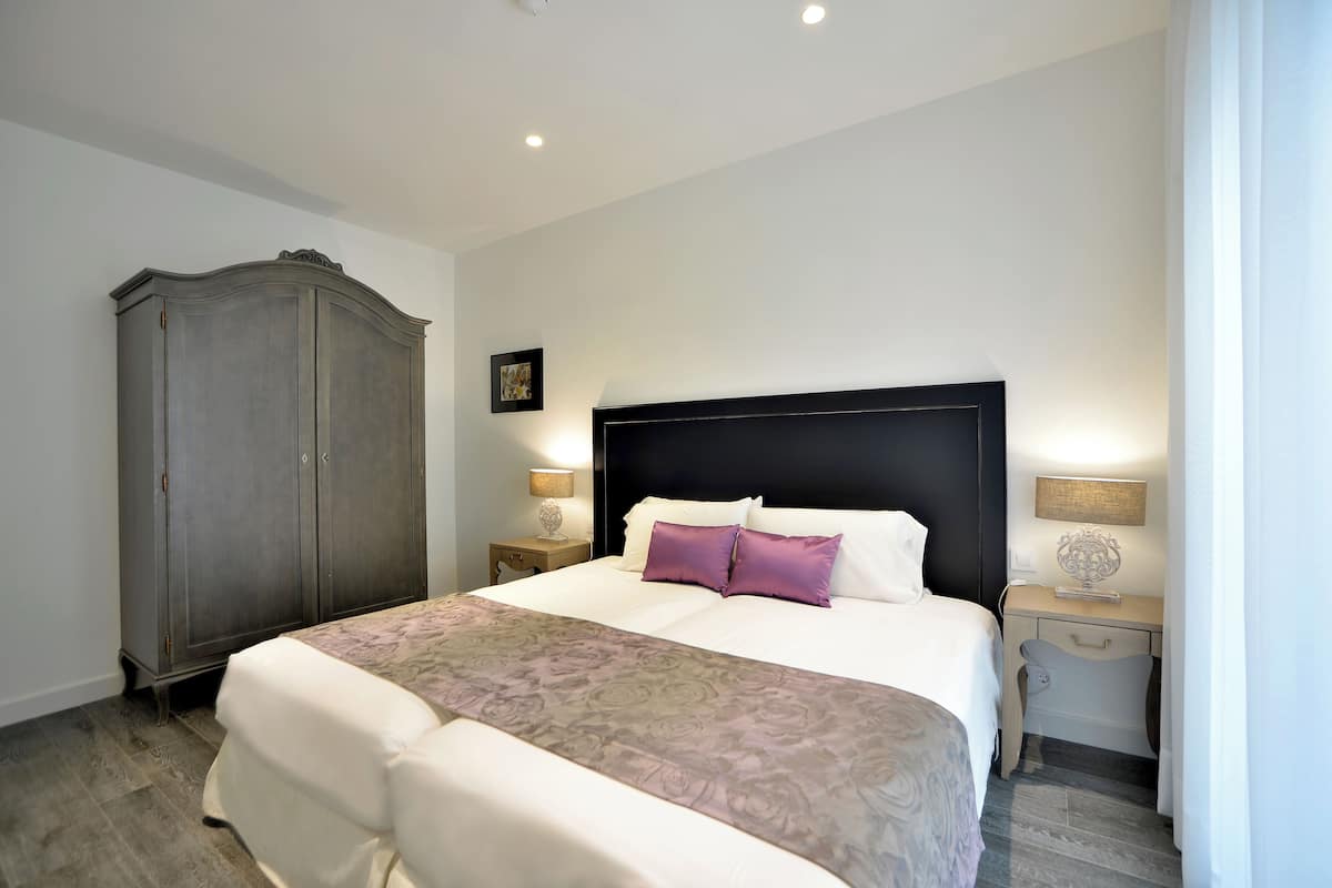 Quarto de hotel com uma cama grande, um guarda-roupa, uma escrivaninha com abajur e um quadro na parede.
