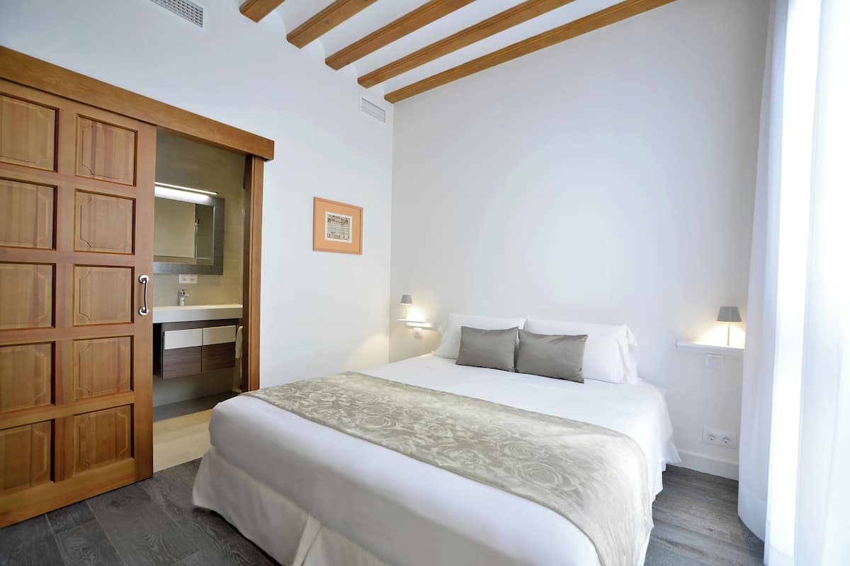 Quarto com cama grande, guarda-roupa de madeira e banheiro visível por uma porta aberta.