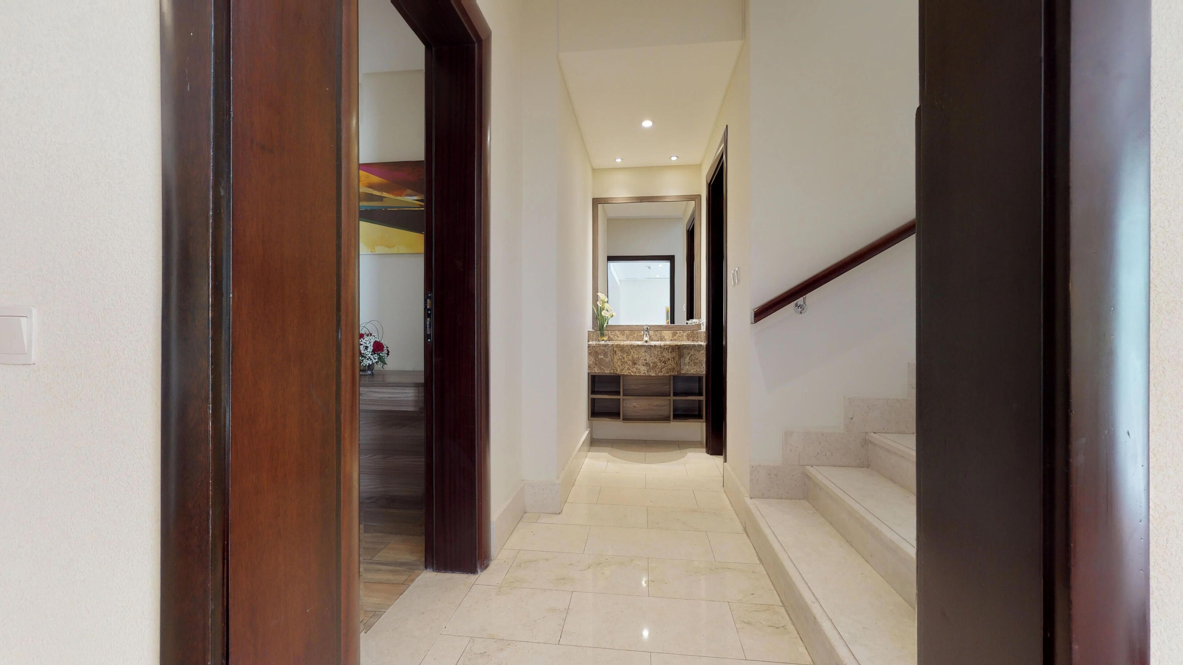 Um corredor com piso de mármore, moldura de porta em madeira e escada com corrimão de madeira.