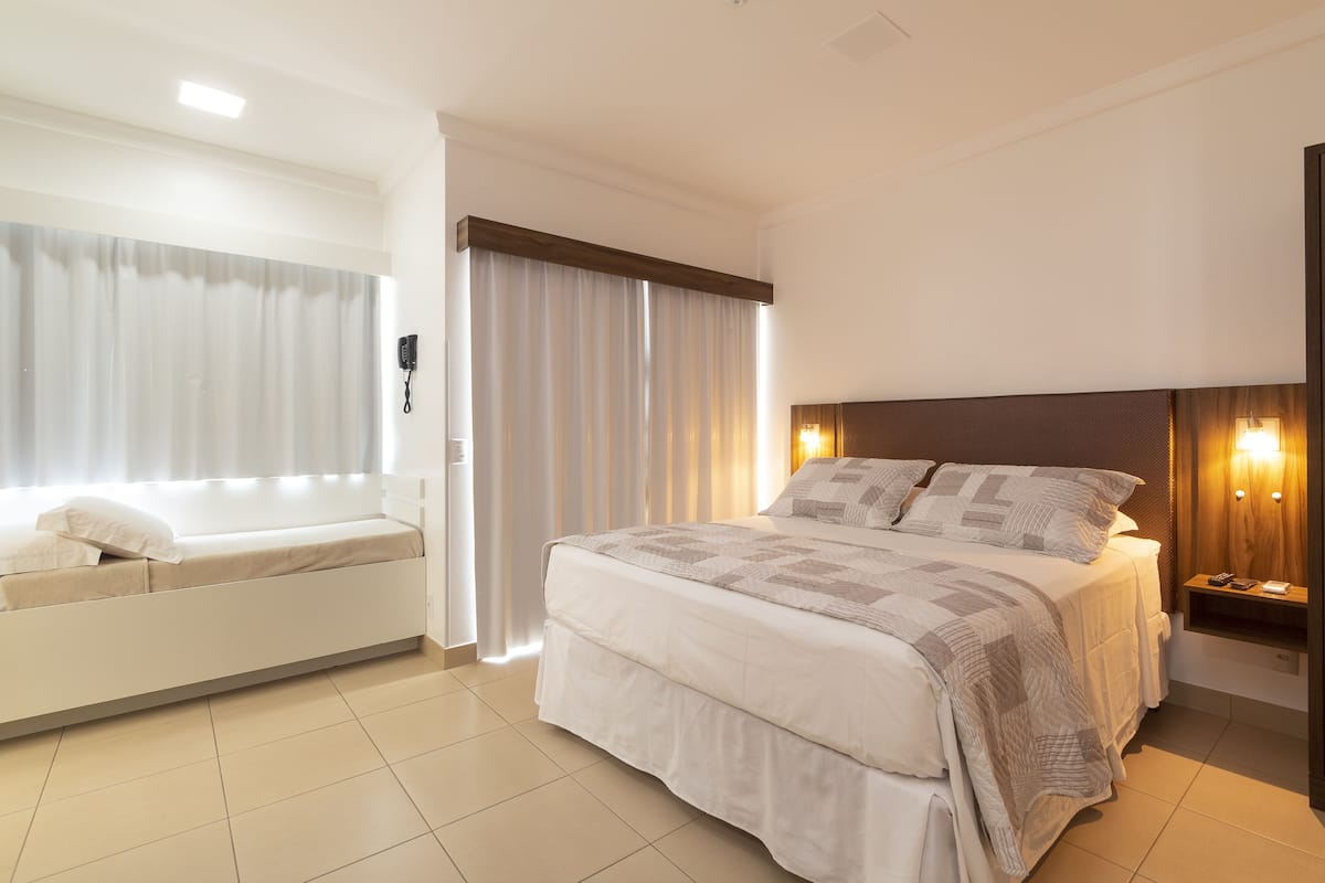 Quarto moderno com cama, mesa de cabeceira e janela com cortinas.