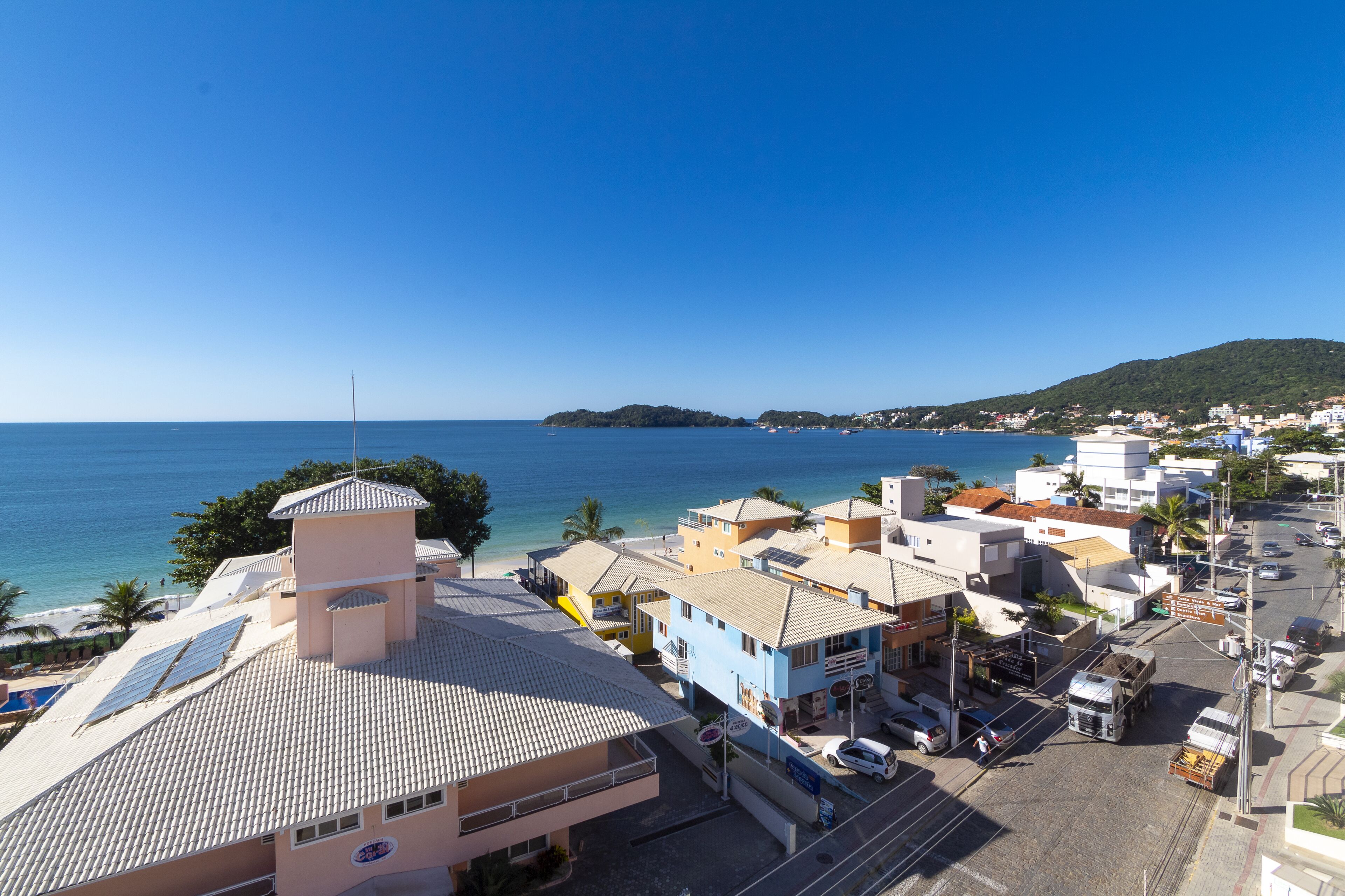 Uma cidade costeira com edifícios, céu azul claro e o mar ao fundo.