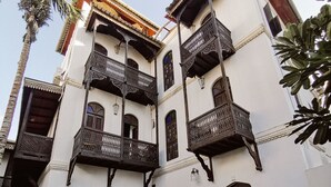 Um edifício tradicional com várias varandas, um pátio com plantas em vasos e uma palmeira.
