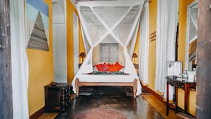 Quarto com cama sob dossel, uma mesinha e um armário de madeira.