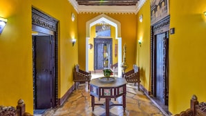 Um corredor com paredes amarelas, portas ornamentadas e chão de pedra.
