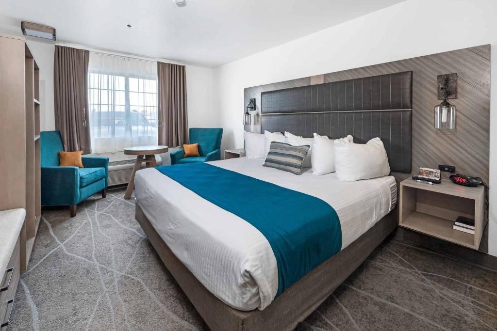 Quarto de hotel com uma cama grande, uma escrivaninha, uma cadeira e uma janela com cortinas.