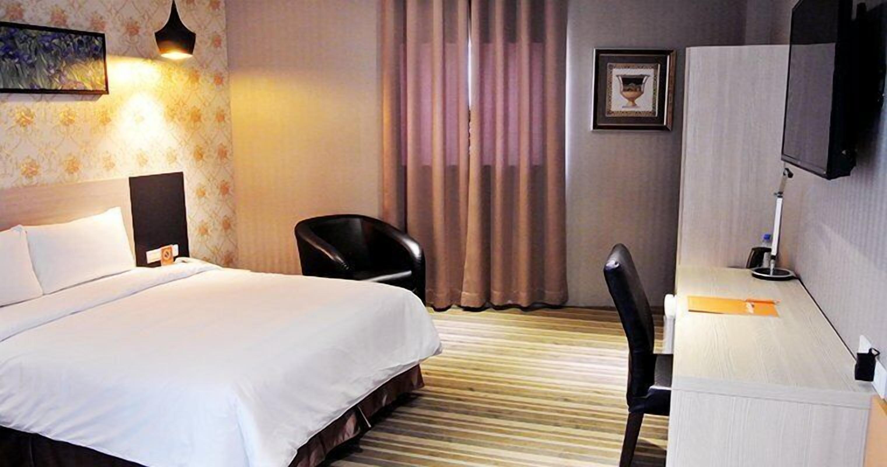 Quarto de hotel com cama, escrivaninha, cadeira, televisão e janela com cortinas.