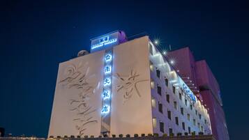 Um hotel com fachada moderna, sinalização iluminada e um grande letreiro vertical com caracteres chineses.