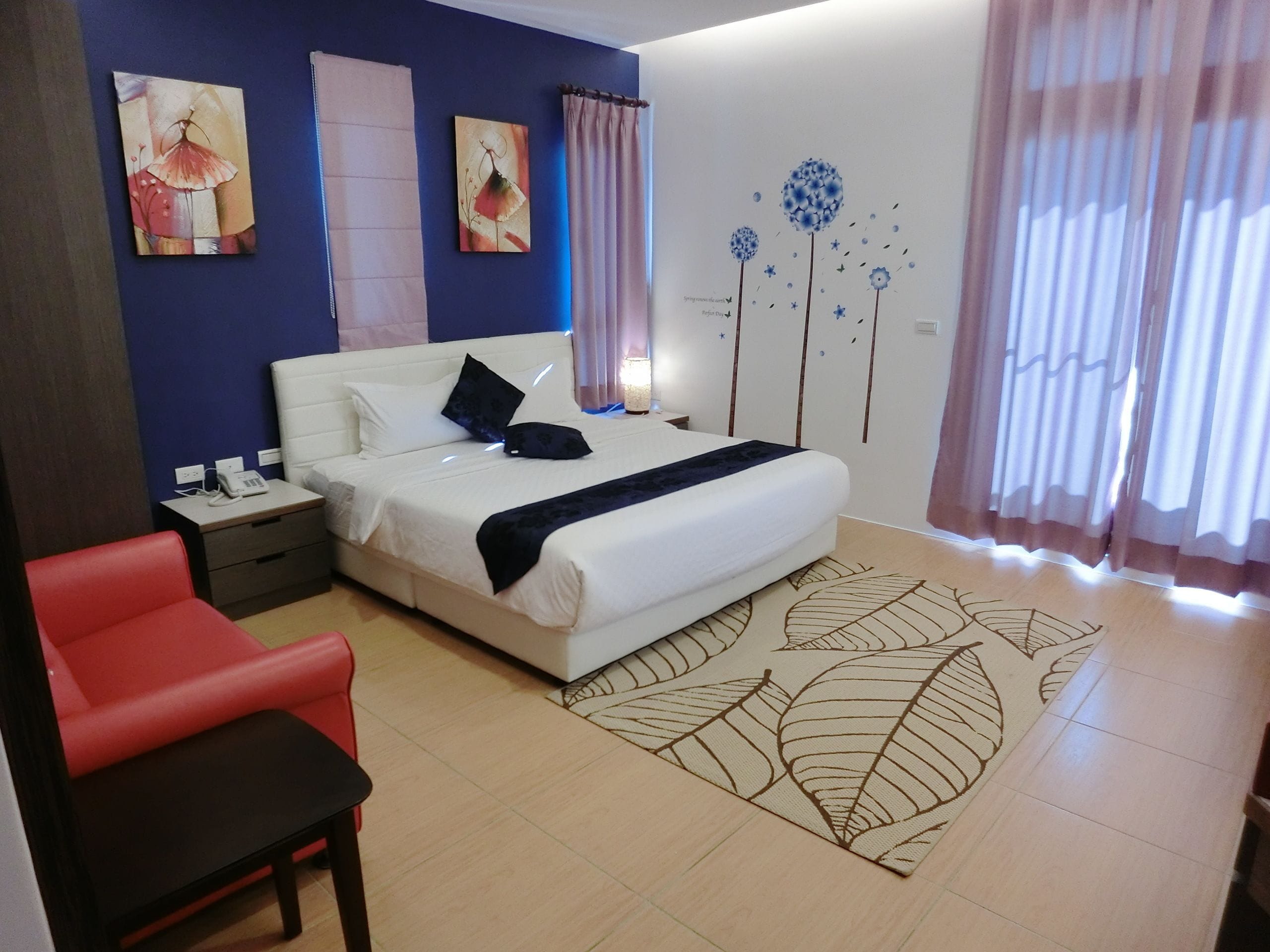 Quarto com cama, mesa de cabeceira, cadeira vermelha e escrivaninha.