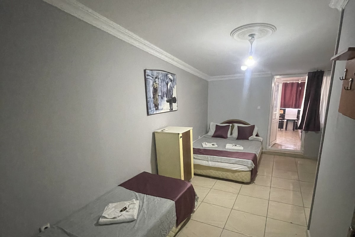 Quarto em dormitório com duas camas individuais, uma mesa pequena e uma cadeira.