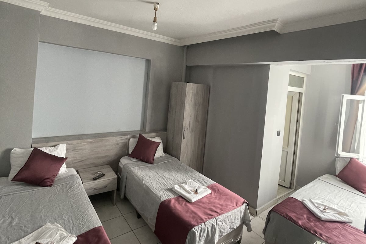 Quarto de hotel com três camas, um guarda-roupa e uma pequena mesa.