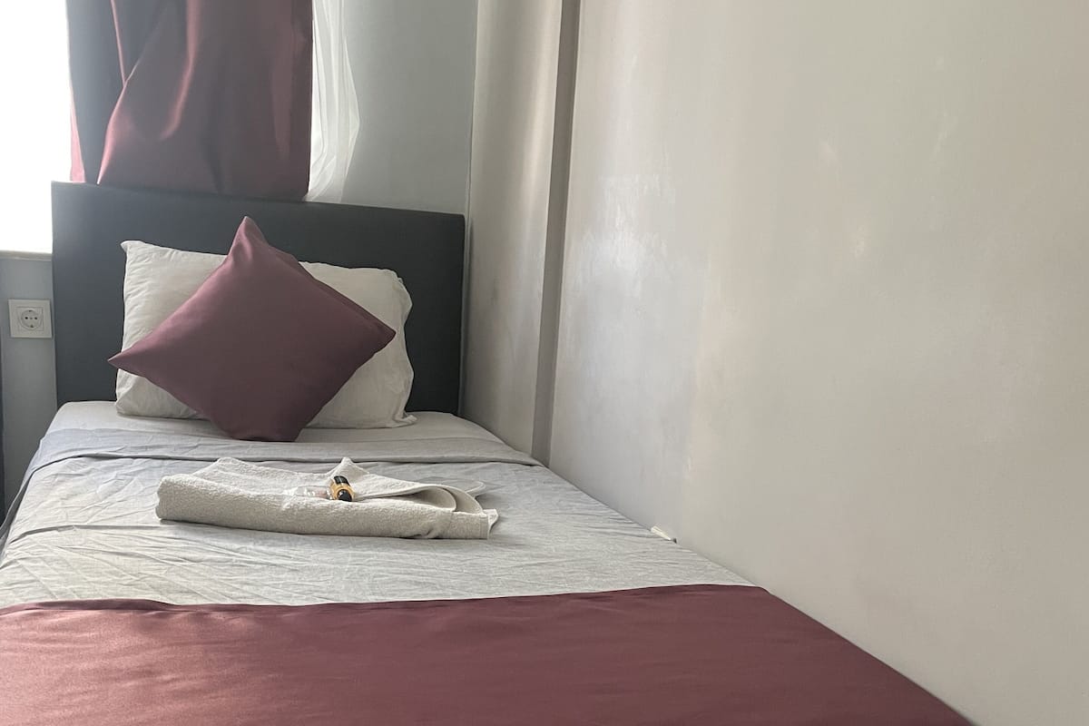 Uma cama bem arrumada com colcha branca e vinho, duas almofadas e uma toalha dobrada.