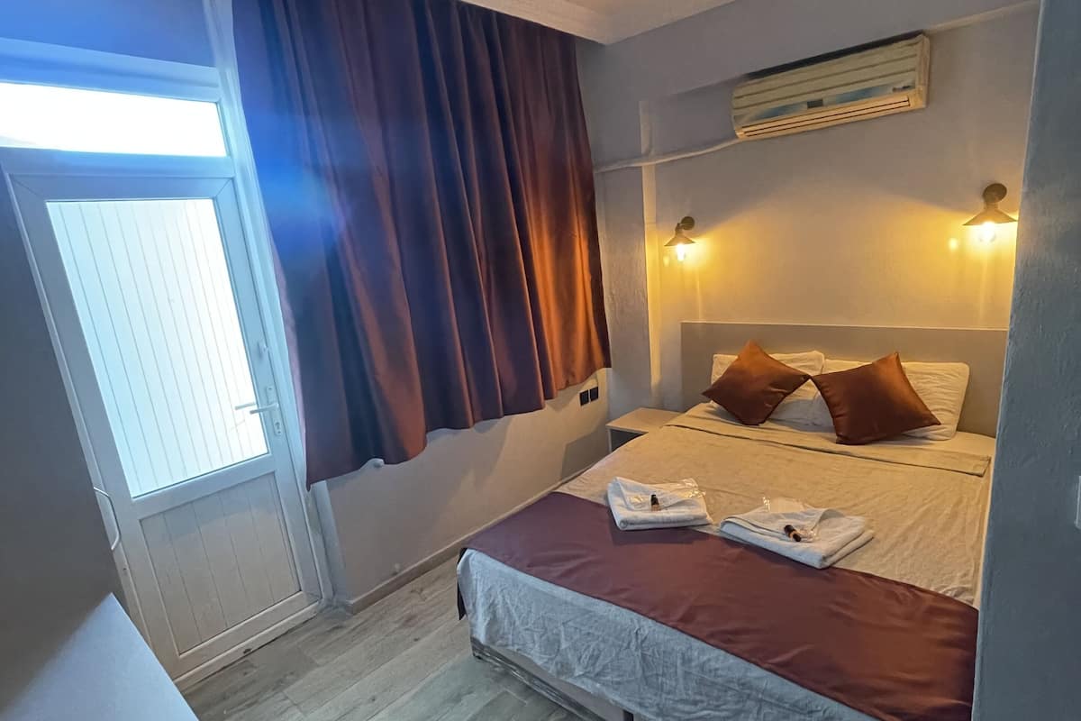 Quarto com cama, janela com cortinas, mesa de cabeceira e ar condicionado fixado na parede.