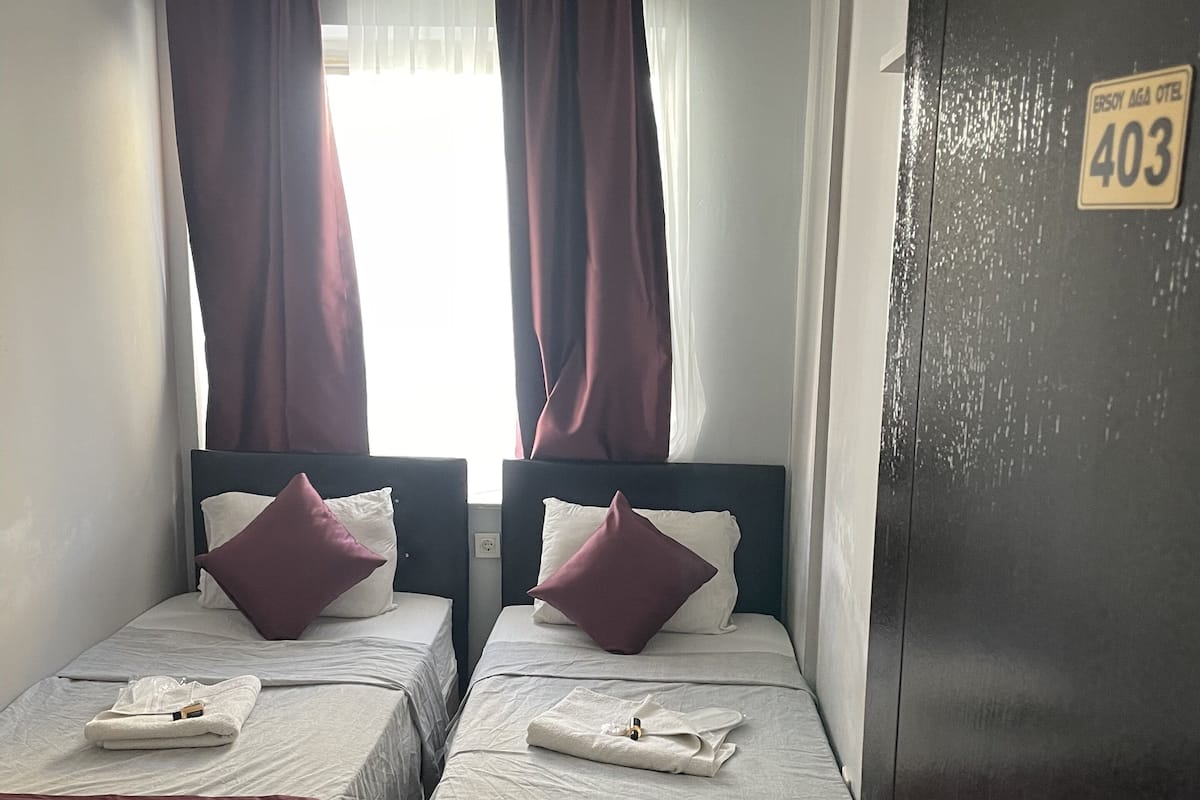 Quarto com duas camas, cada uma com travesseiro e toalha dobrada. Há uma porta com o símbolo de número.