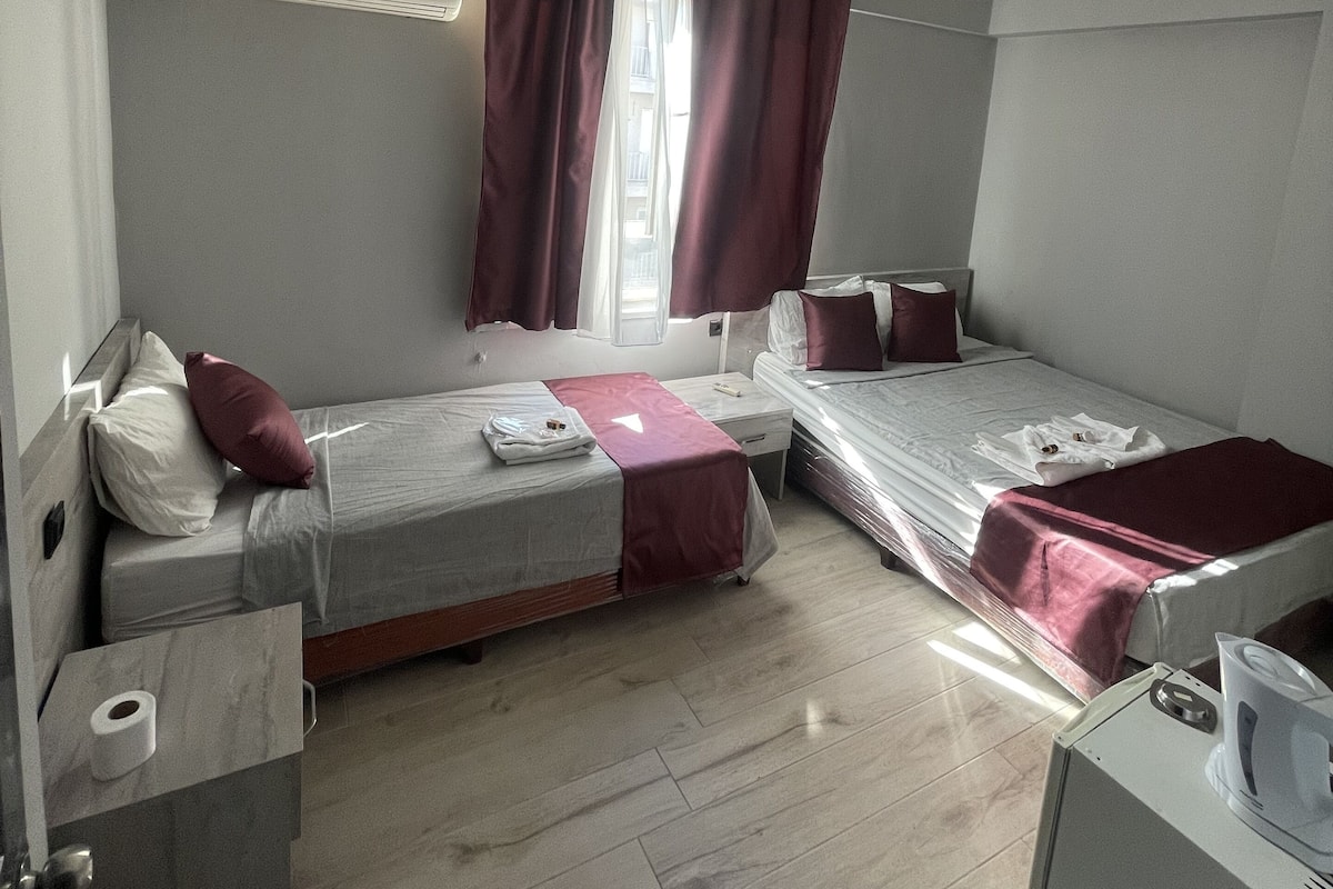 Quarto de hotel compacto com duas camas de solteiro, uma pequena mesa, guarda-roupa embutido e cozinha compacta.
