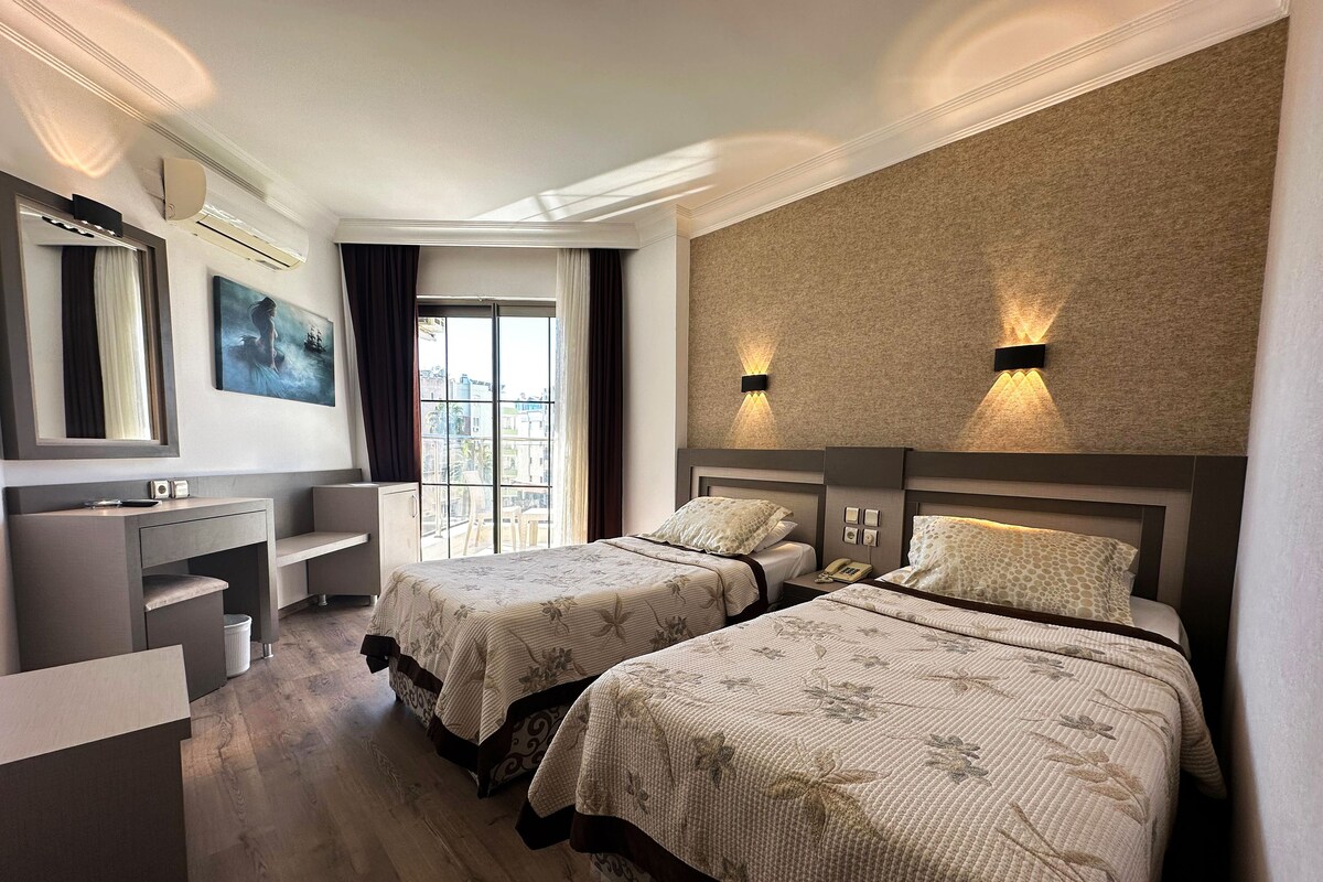 Quarto de hotel moderno com duas camas, uma escrivaninha, toucador e uma janela grande com cortinas.