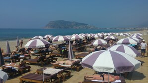 Uma praia com muitos espreguiçadeiras e guarda-sóis listrados em roxo e branco.