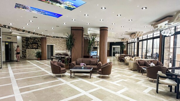 Um lobby amplo com teto alto, iluminação embutida e área de estar central com sofás e poltronas.