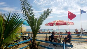 Restaurante à beira-mar com mesas ao ar livre, palmeiras e bandeiras.