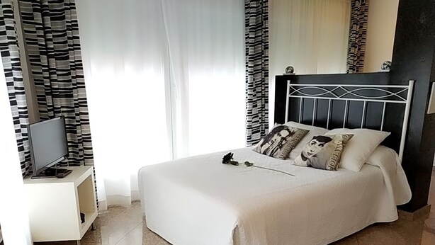 Quarto de hotel bem arrumado com cama, televisão sobre um suporte e janela com cortinas.