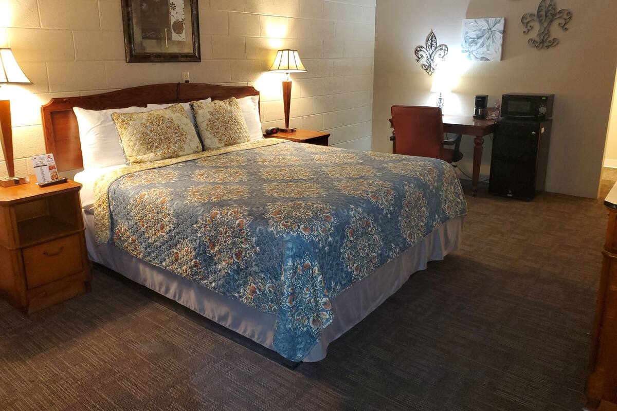 Um quarto bem arrumado com uma cama grande, duas mesas de cabeceira com luminárias, uma pequena escrivaninha com um computador e arte decorativa na parede.