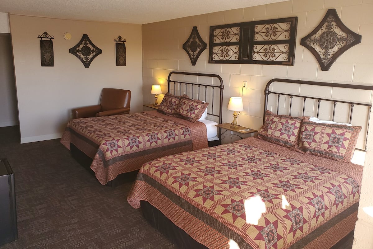 Quarto de hotel com duas camas, uma cadeira e arte decorativa na parede.