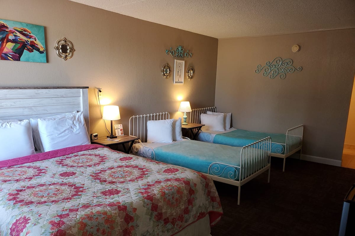 Quarto de hotel com duas camas, cabeceira de madeira, mesas de cabeceira com luminárias, decoração na parede e piso coberto por carpete.