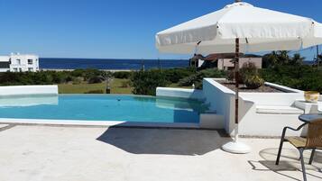 Uma piscina com vista para o mar, um guarda-sol branco e uma cadeira.