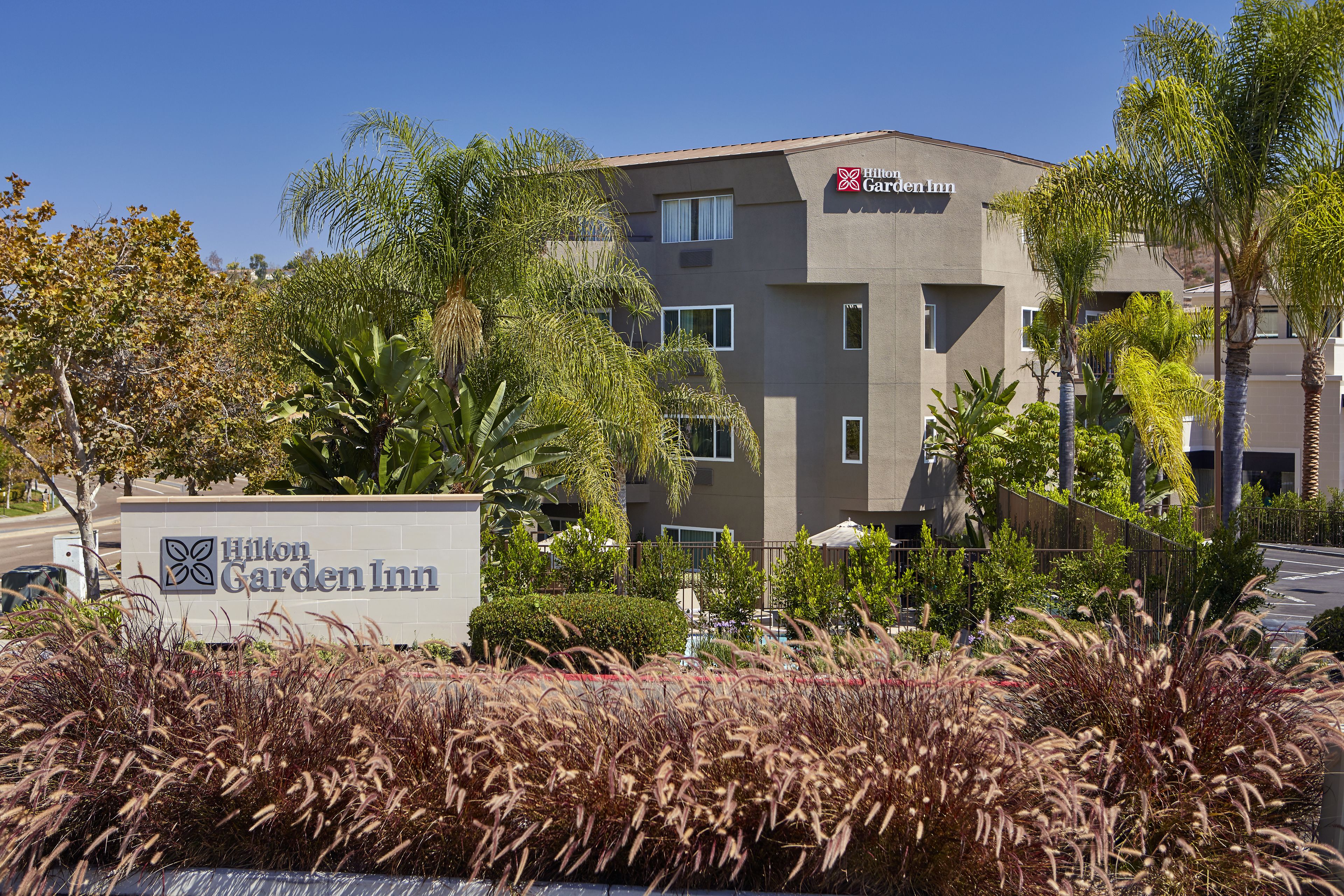 Um Hilton Garden Inn com um edifício moderno e uma área de entrada ajardinada.