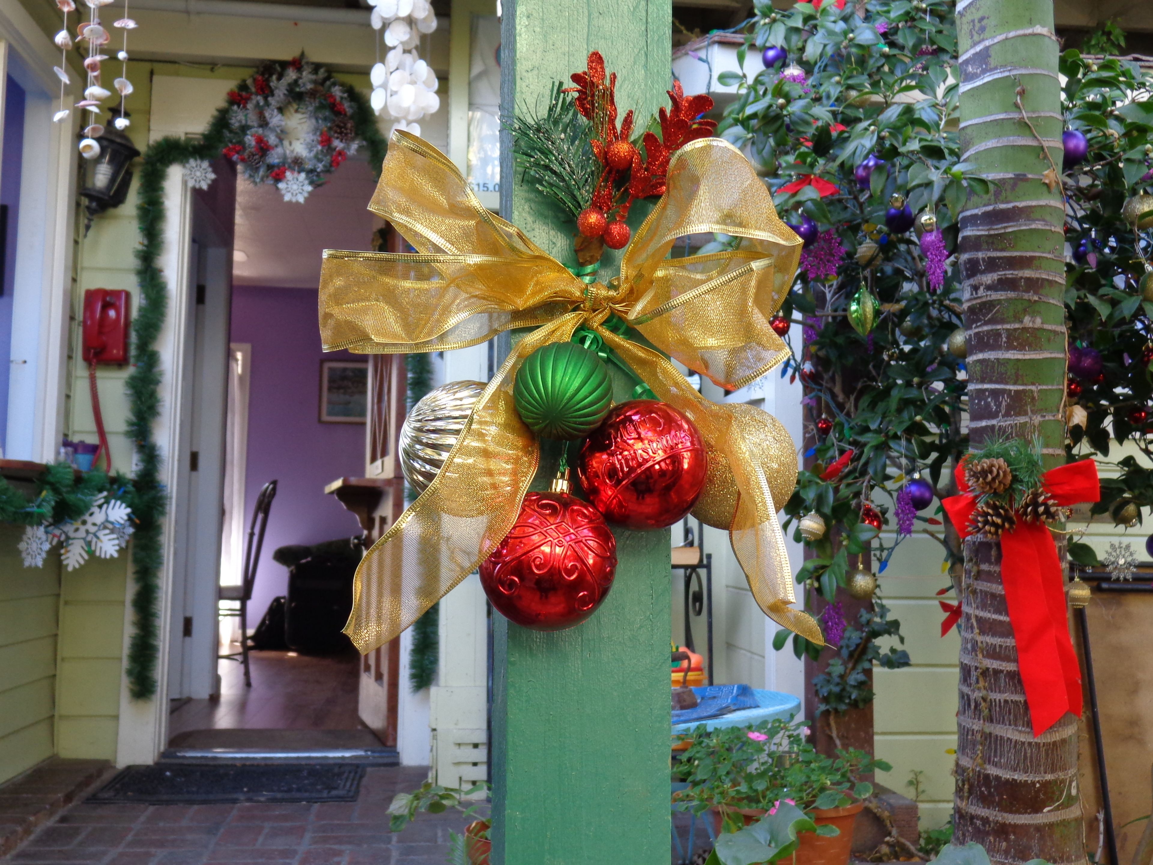 Uma entrada decorada com um grande laço dourado, enfeites vermelhos e verdes e uma coroa de louros.